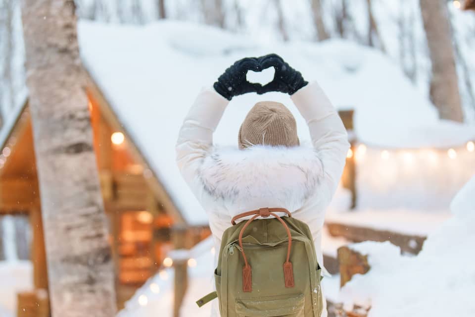 Uma pessoa em uma floresta nevada, com uma cabana ao fundo.