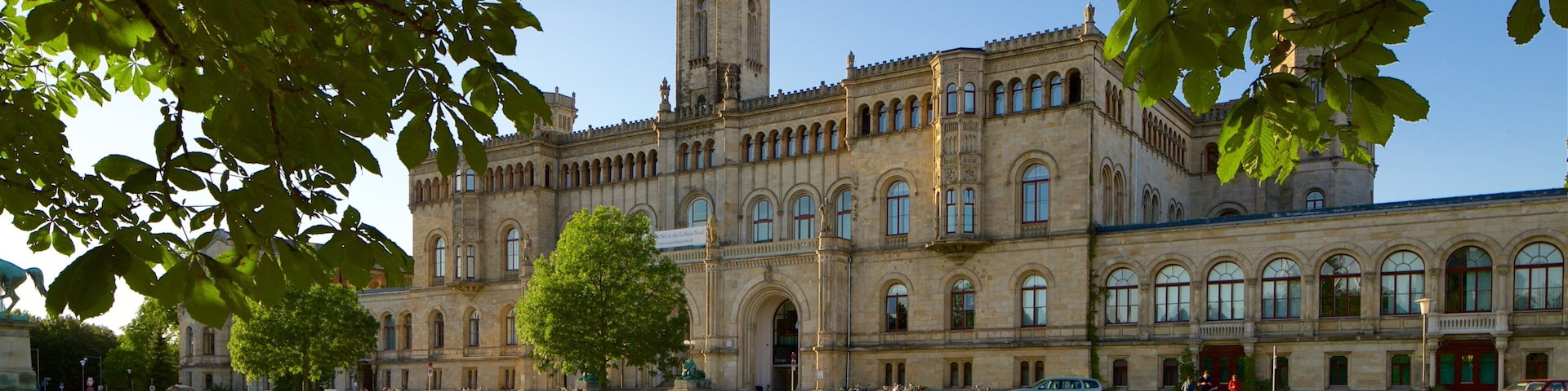 Um edifício histórico com uma torre imponente, rodeado por um gramado bem cuidado e árvores.