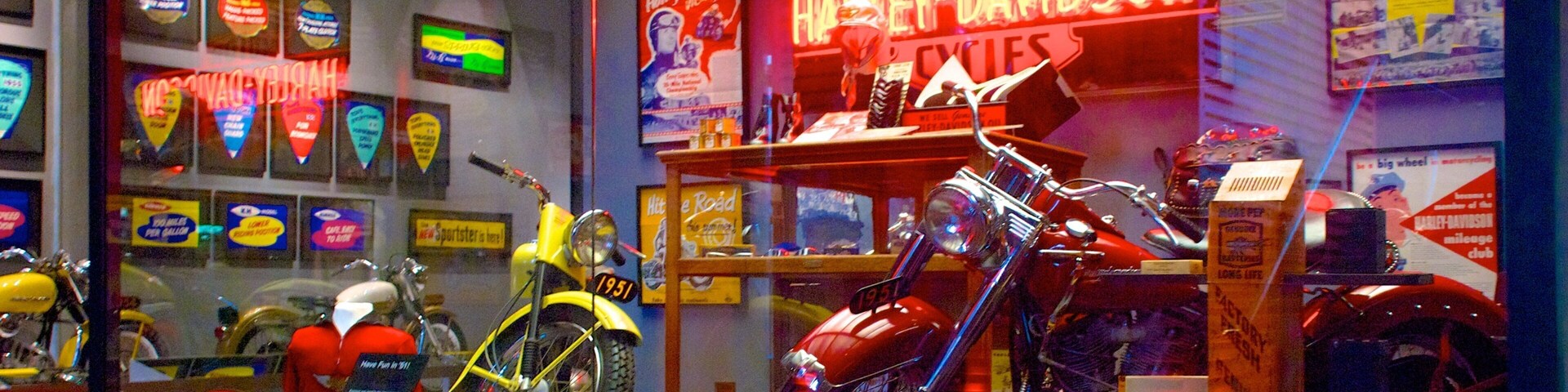 Uma loja de motocicletas com diversos modelos em exposição, incluindo uma Big Twin vermelha de 1951.