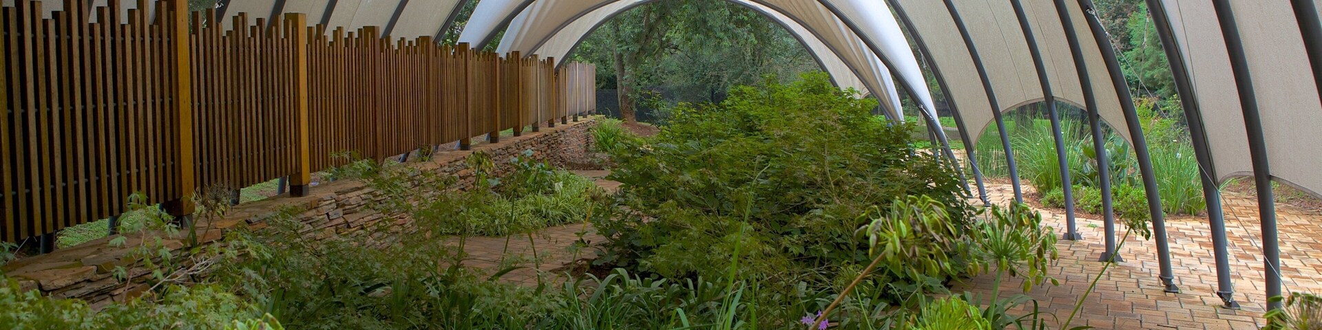 Uma estrutura em forma de túnel, com cerca de madeira e caminho de tijolos, cercada por vegetação.