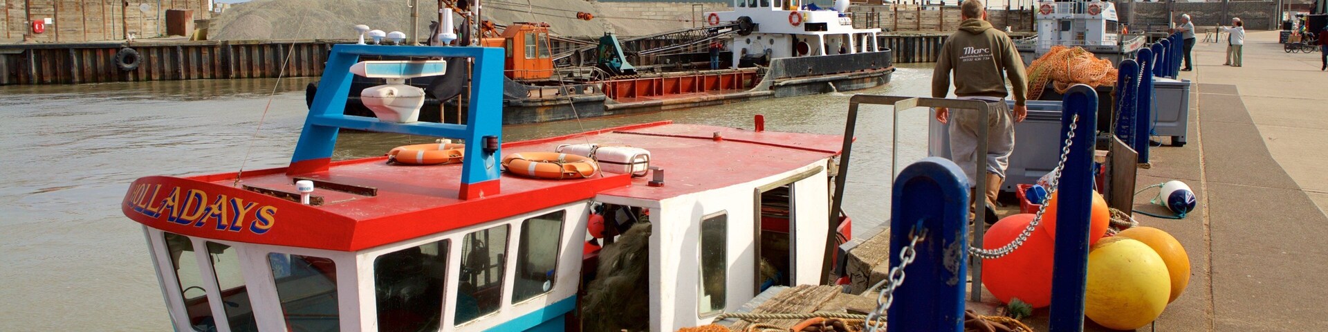 Um cais com um barco vermelho e azul chamado "HOLLADAYS" e redes de pesca laranja.