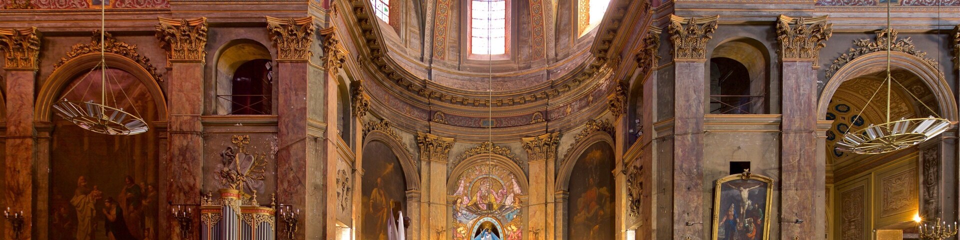 Interior de igreja ornamentado, com altar central, janelas de vitrais e detalhes artísticos no teto.