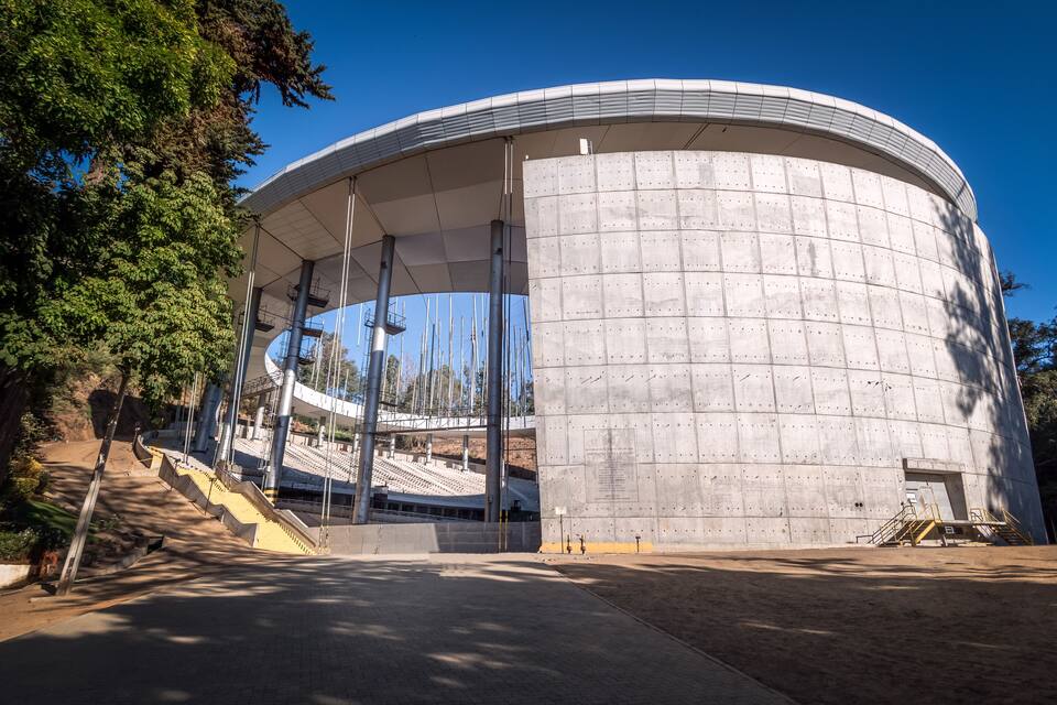 Um edifício grande e circular com um telhado curvo, cercado por árvores e uma escadaria que leva até ele.