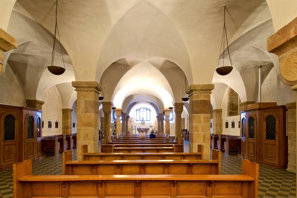 Interior de igreja com tetos em arco, bancos de madeira e colunas de pedra.