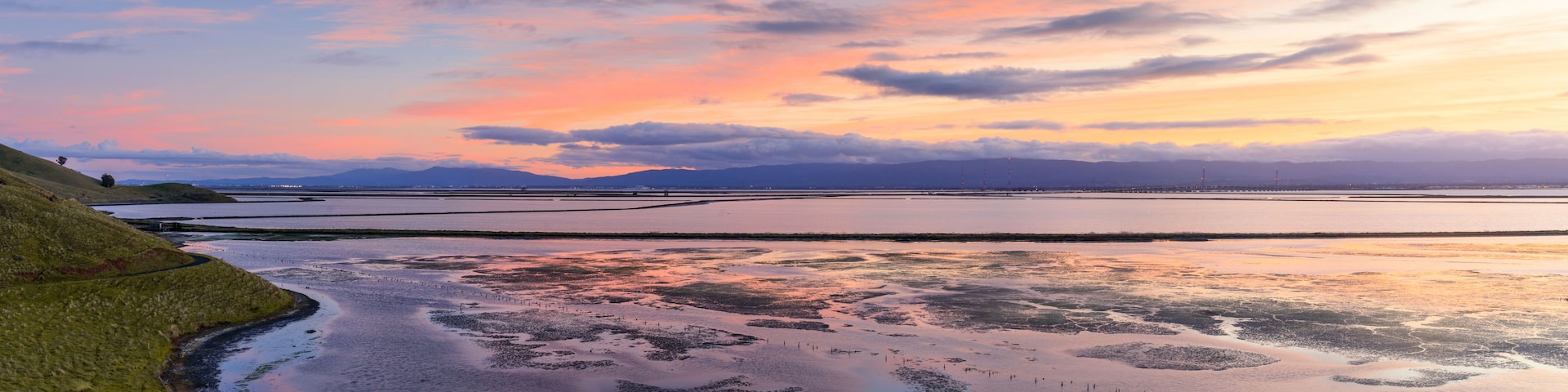Paisagem costeira com um pôr do sol, uma colina gramada e um mar tranquilo.