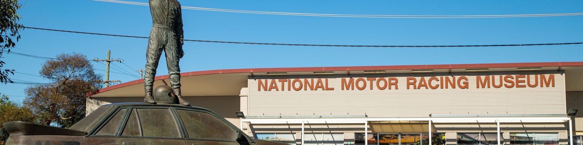 Uma estátua de uma pessoa segurando um megafone em frente a um edifício com a placa "National Motor Racing Museum".