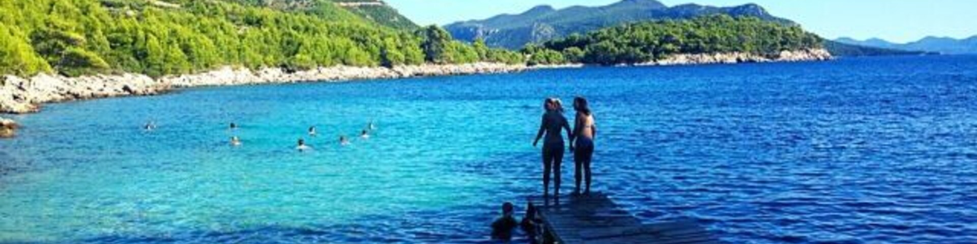 Um cais de madeira que se estende por um mar azul e límpido, com pessoas na extremidade.