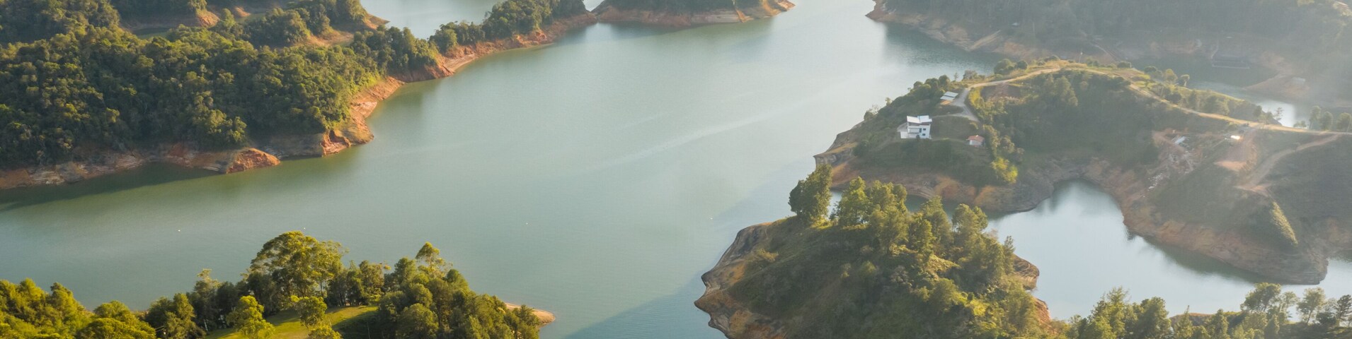 Um rio serpenteando por um vale arborizado, com uma formação rochosa imponente ao longe.
