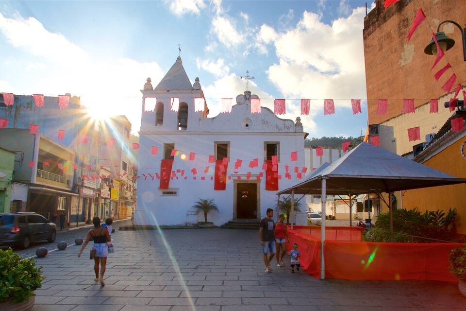 Uma rua com uma igreja branca, bandeiras vermelhas e uma área de mercado.