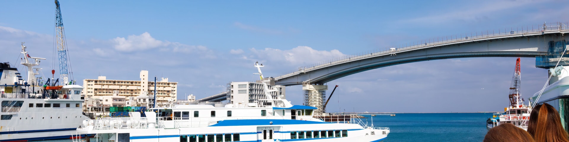 Um ferry com listras azuis e brancas atracado perto de uma ponte e edifícios ao fundo.