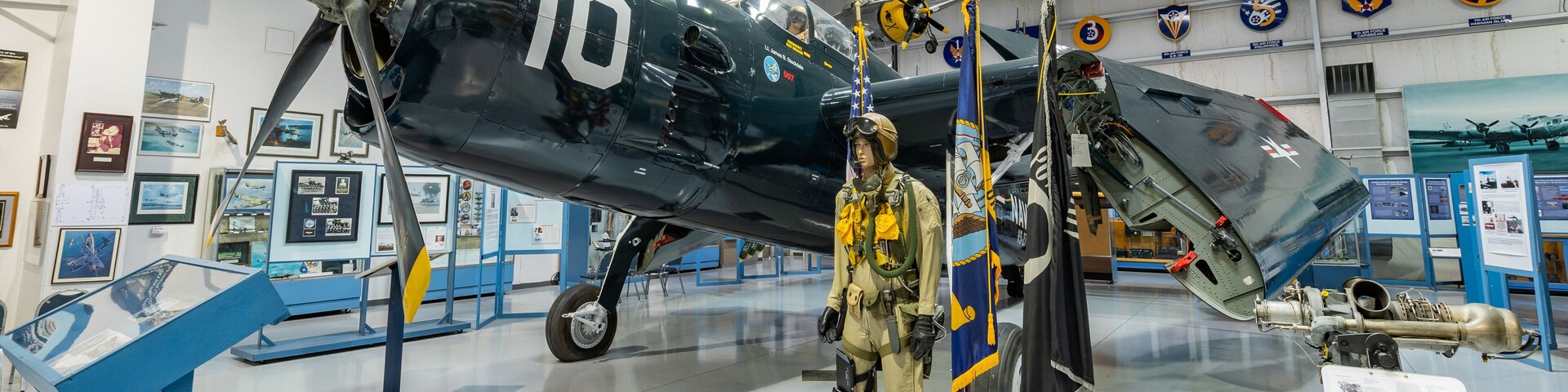 Uma aeronave militar antiga com o número 10 na lateral, um manequim de piloto e diversos símbolos militares nas paredes.