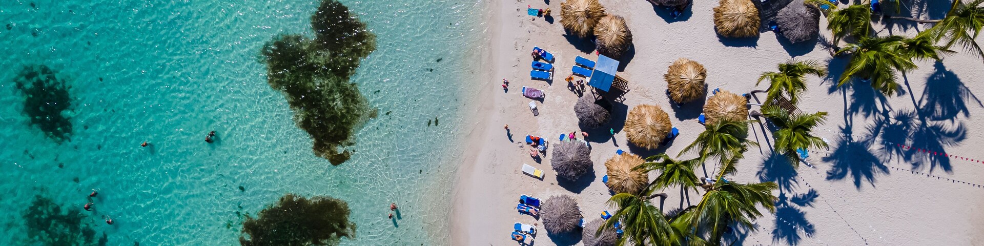 Uma praia com águas turquesa cristalinas, guarda-sóis de palha e palmeiras.