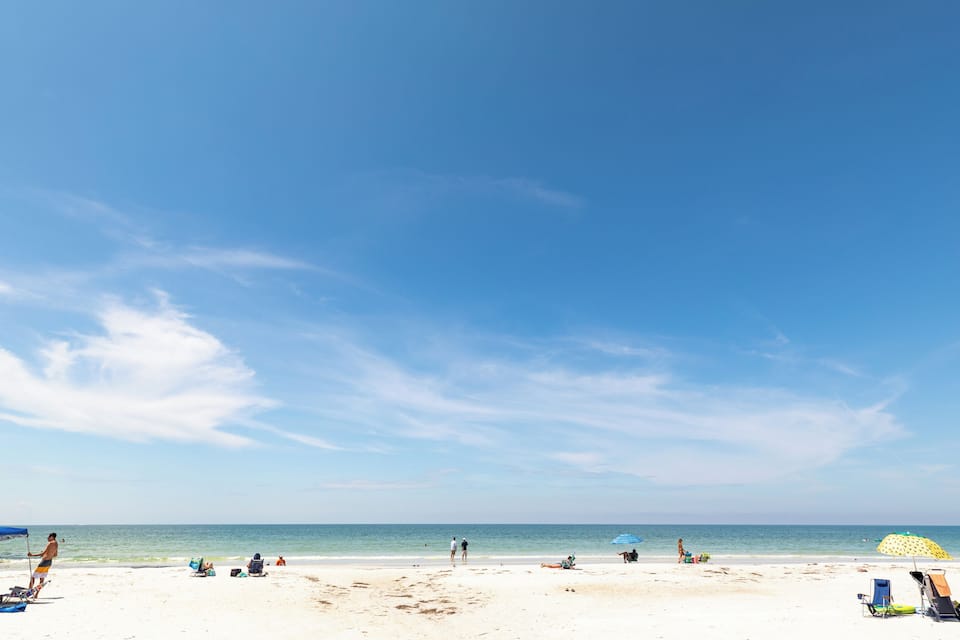 Uma praia com pessoas se bronzeando, guarda-sóis e cadeiras de praia.