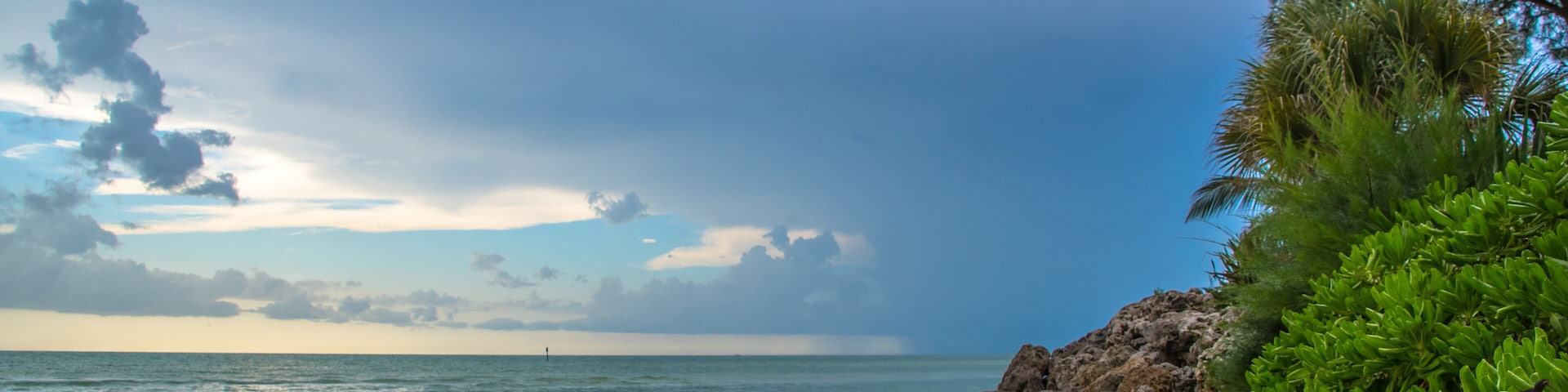 Uma praia com céu claro, mar calmo e formações rochosas.