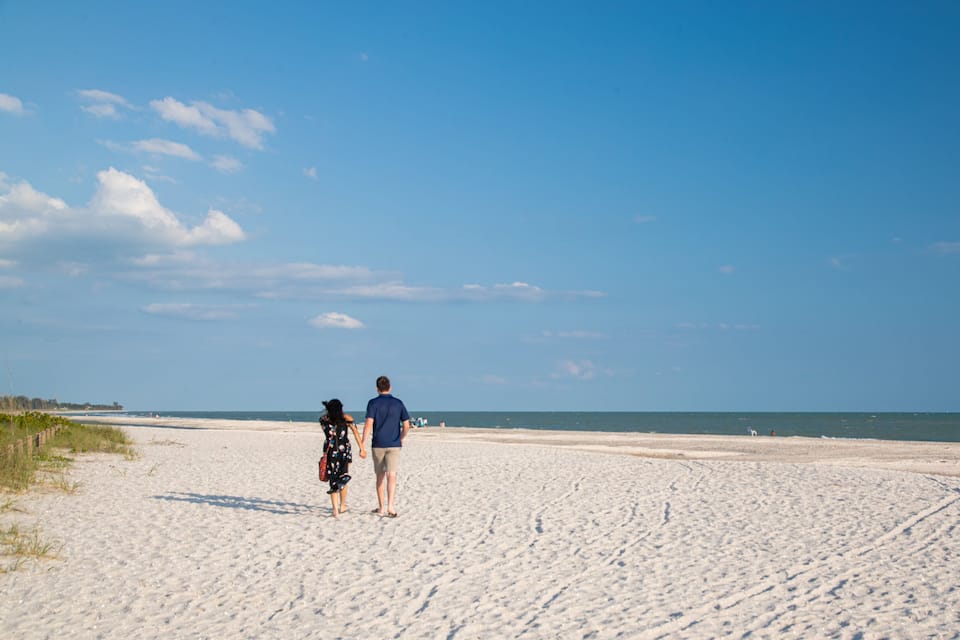 Uma praia de areia com céu claro e oceano ao fundo.