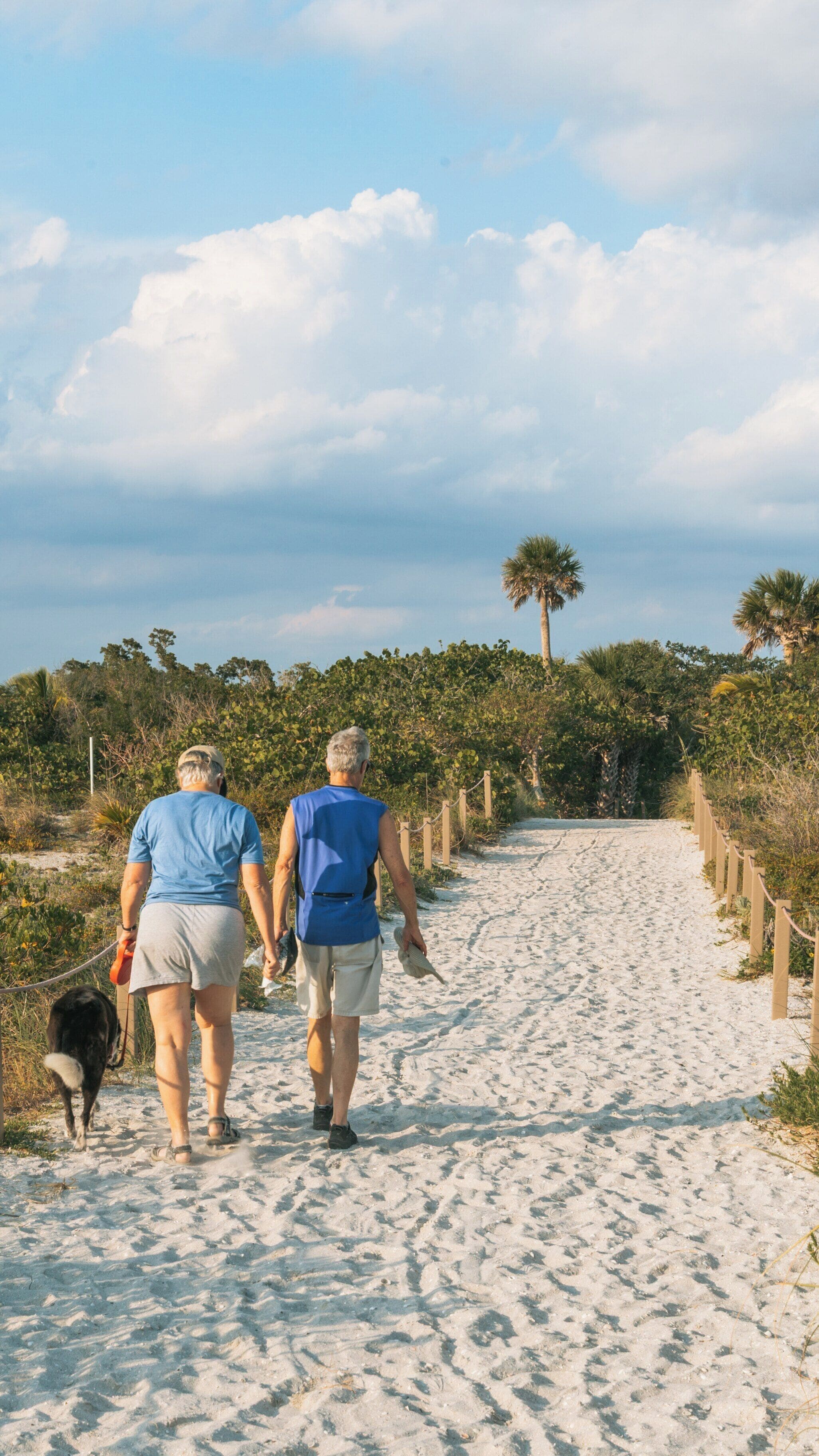 Couple enjoys a leisurely walk along Bowman's Beach in Fort Myers, Florida, under a cloudy sky with their dog