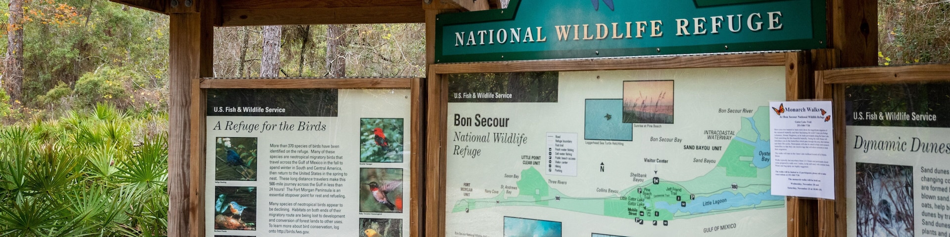 Uma placa de madeira com 'Bon Secour National Wildlife Refuge' e painéis informativos sobre espécies de aves e um mapa.