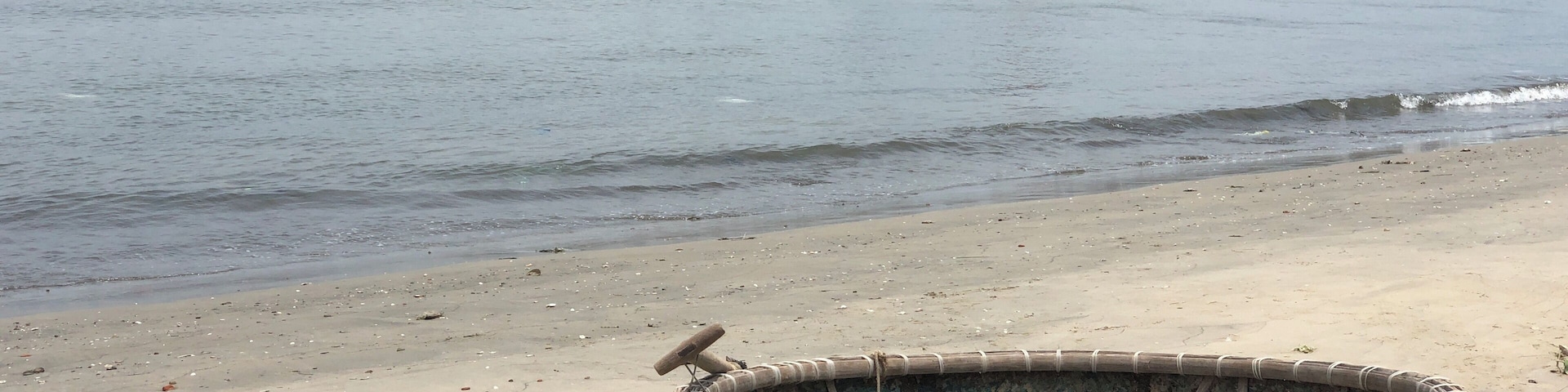 Uma praia com um barco azul grande em primeiro plano e vários barcos menores ao fundo.
