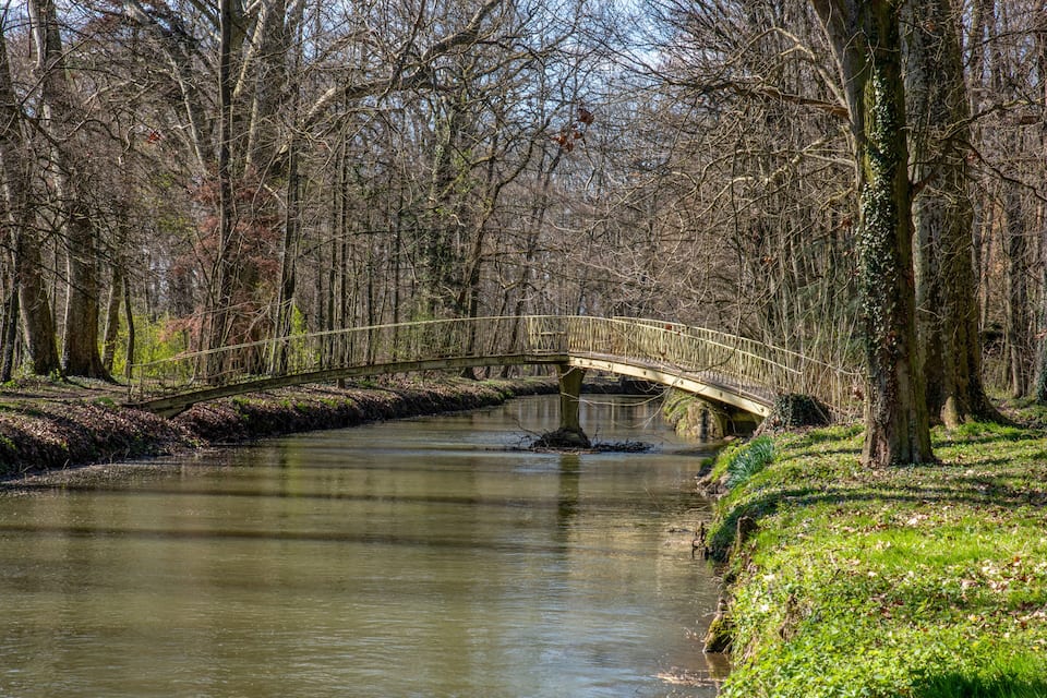 Uma ponte de pedra sobre um rio calmo, rodeada por árvores.