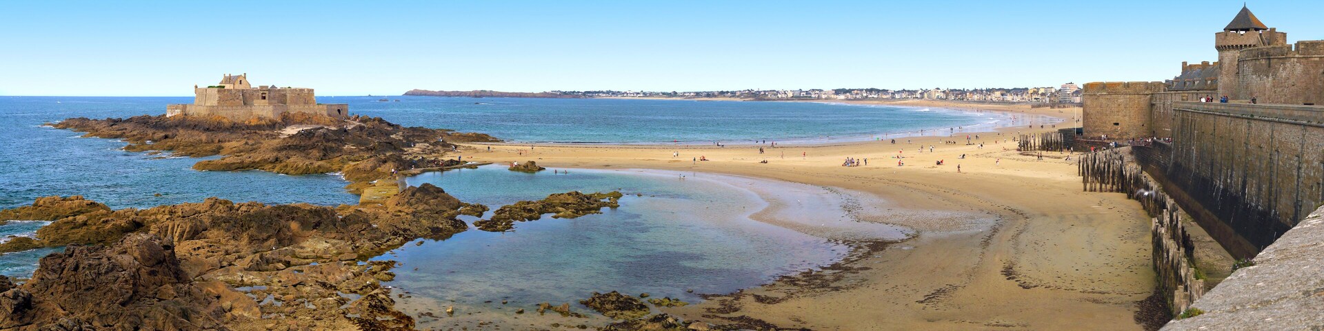 Uma vila costeira com um castelo histórico, uma praia de areia e falésias rochosas.