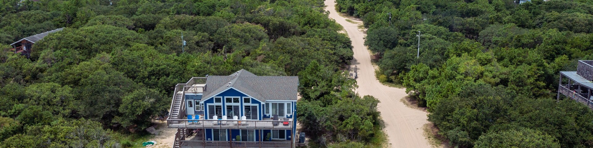 Uma casa à beira-mar cercada por floresta densa e um caminho de terra.