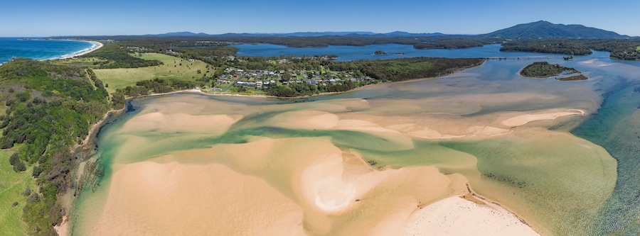 Vista aérea de uma área costeira com praia, águas cristalinas e uma comunidade residencial.