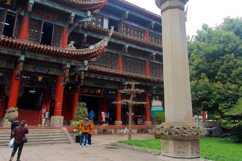 Um edifício tradicional chinês com arquitetura elaborada, um grande pilar de pedra e um jardim bem cuidado.
