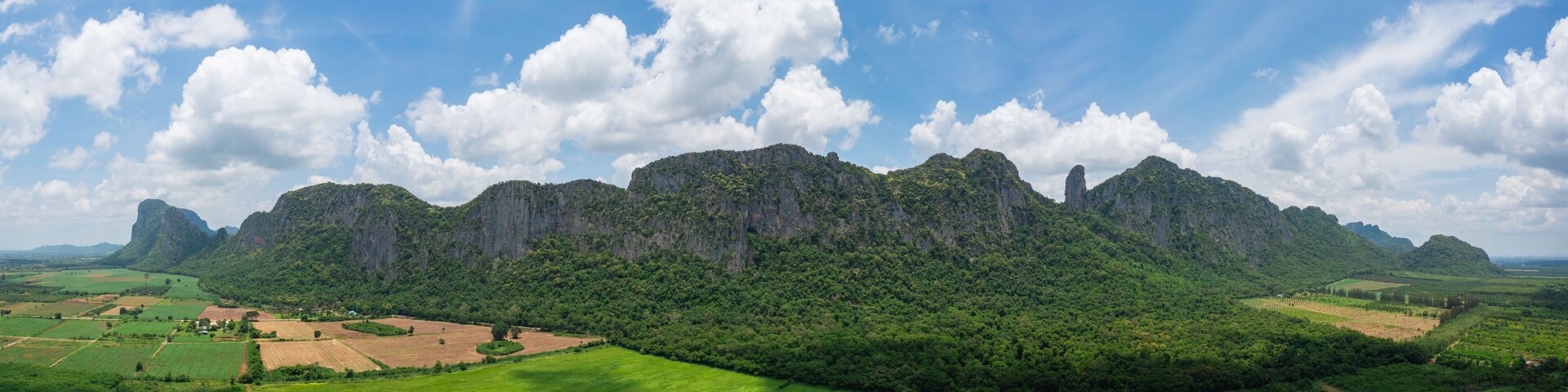 Paisagem montanhosa com campos verdejantes e um céu azul límpido com nuvens.