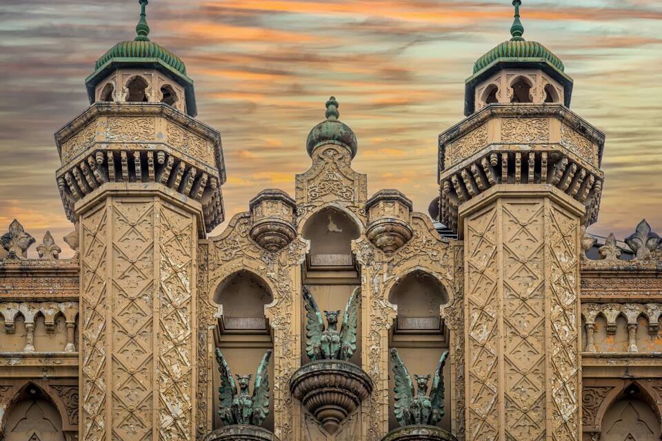 Um edifício histórico com arquitetura ornamentada, apresentando duas torres com cúpulas e esculturas detalhadas.