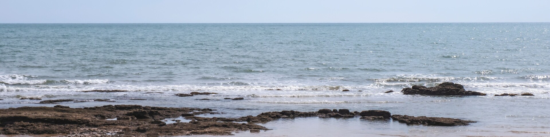 Uma praia com afloramentos rochosos e águas calmas.