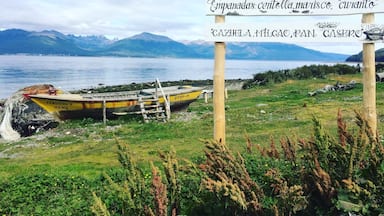 Paisagem costeira com um letreiro listando iguarias locais, um barco e montanhas ao fundo.