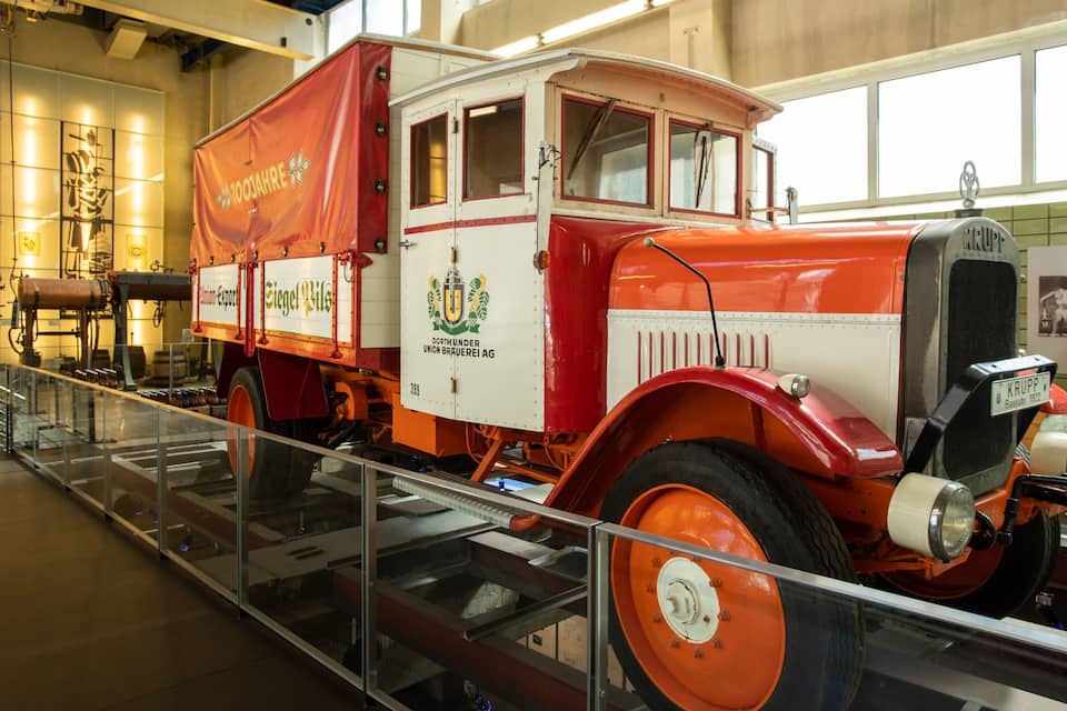 Uma caminhão antiga vermelha e branca com a inscrição 'Dortmunder Union Brauerei AG' e 'Kruppe'.