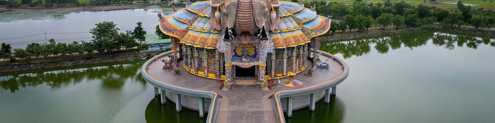 Um templo com uma estátua dourada no topo, rodeado por água e vegetação.