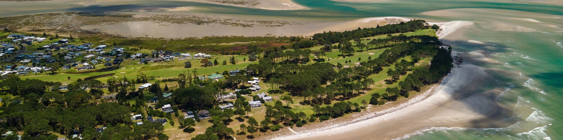 Paisagem costeira com praia, campo de golfe e montanhas ao fundo.