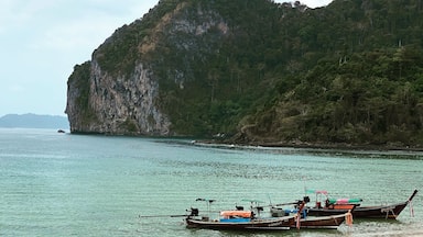 Uma praia com barcos e um penhasco imponente.