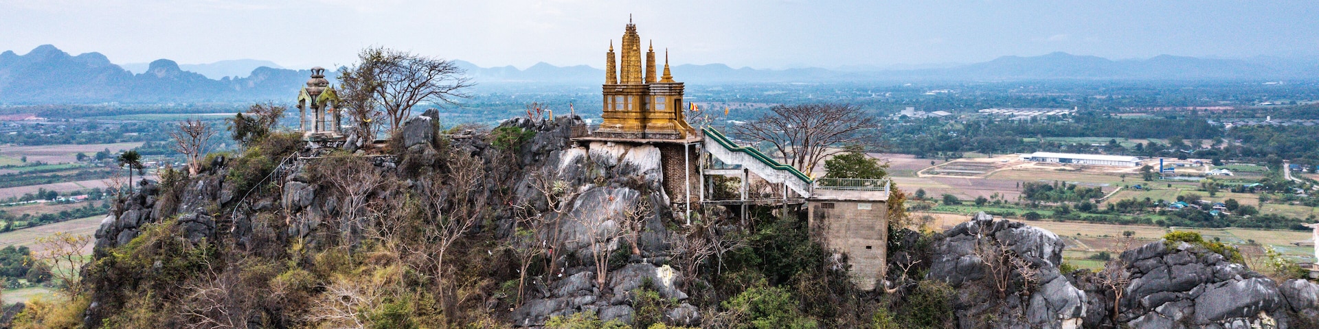 Um templo numa colina rochosa com vista para montanhas e campos distantes.