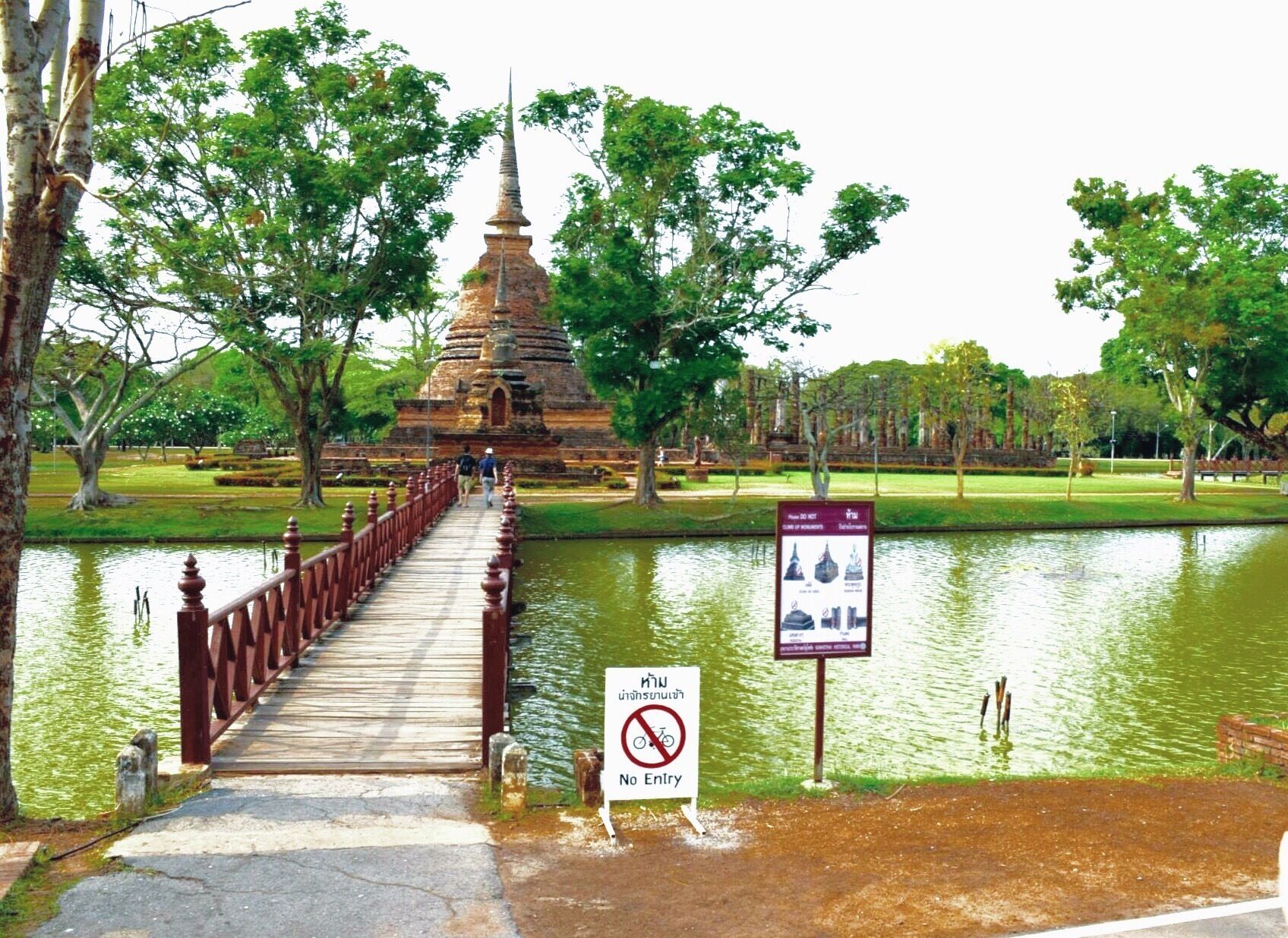 Um templo com um stupa, uma ponte sobre um lago e uma placa de 'Proibido Entrar'.