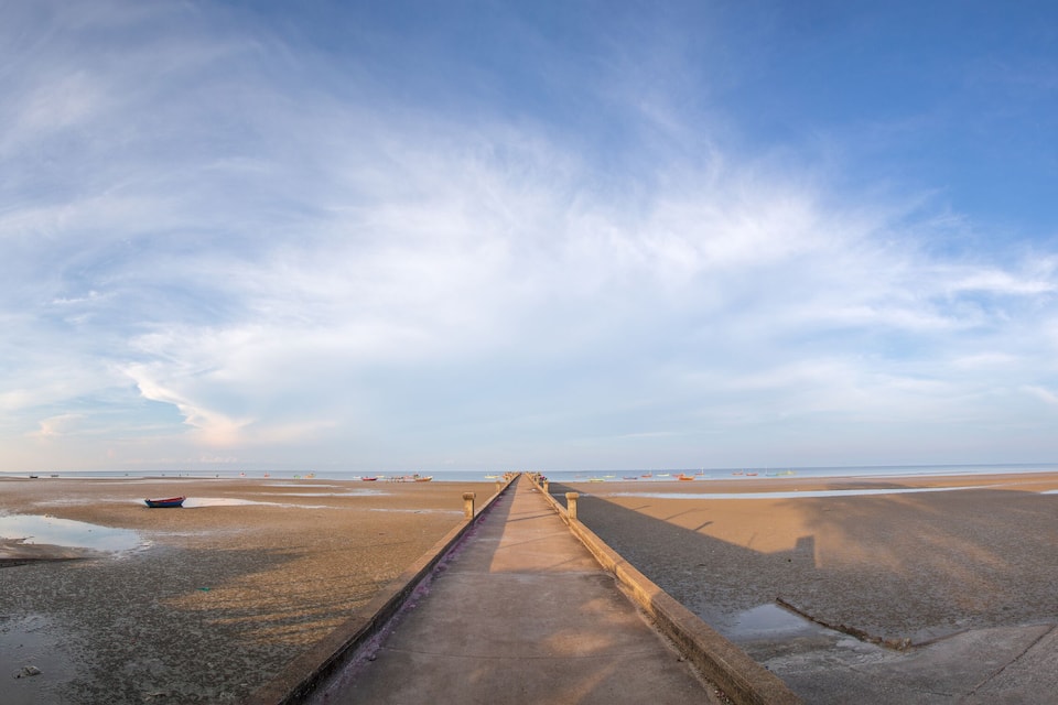 Uma praia com um calçadão de concreto que leva à água, barcos e uma ilha ao longe.