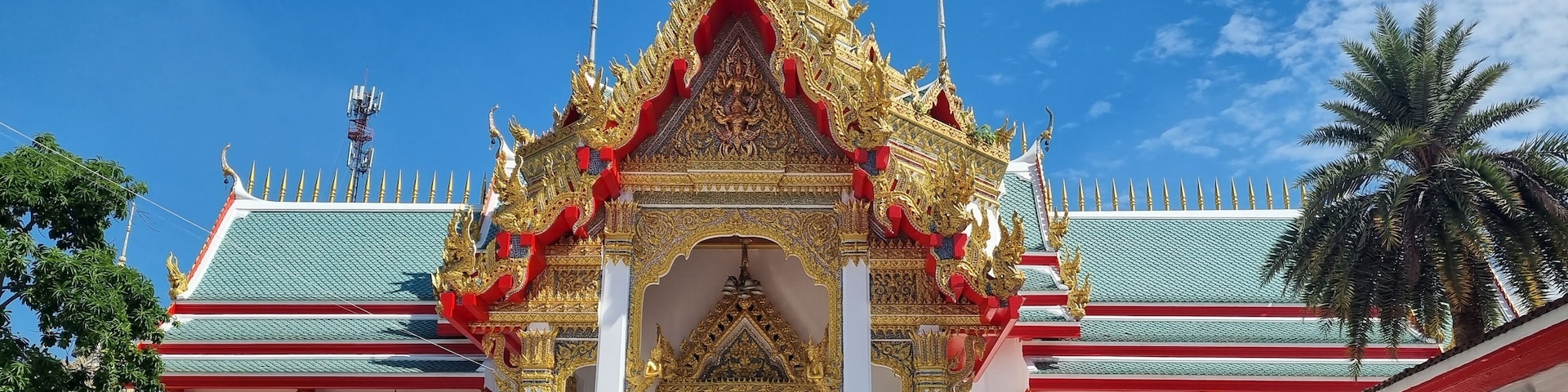 Um templo tradicional tailandês com detalhes dourados ornamentados, telhado verde e fachada branca.