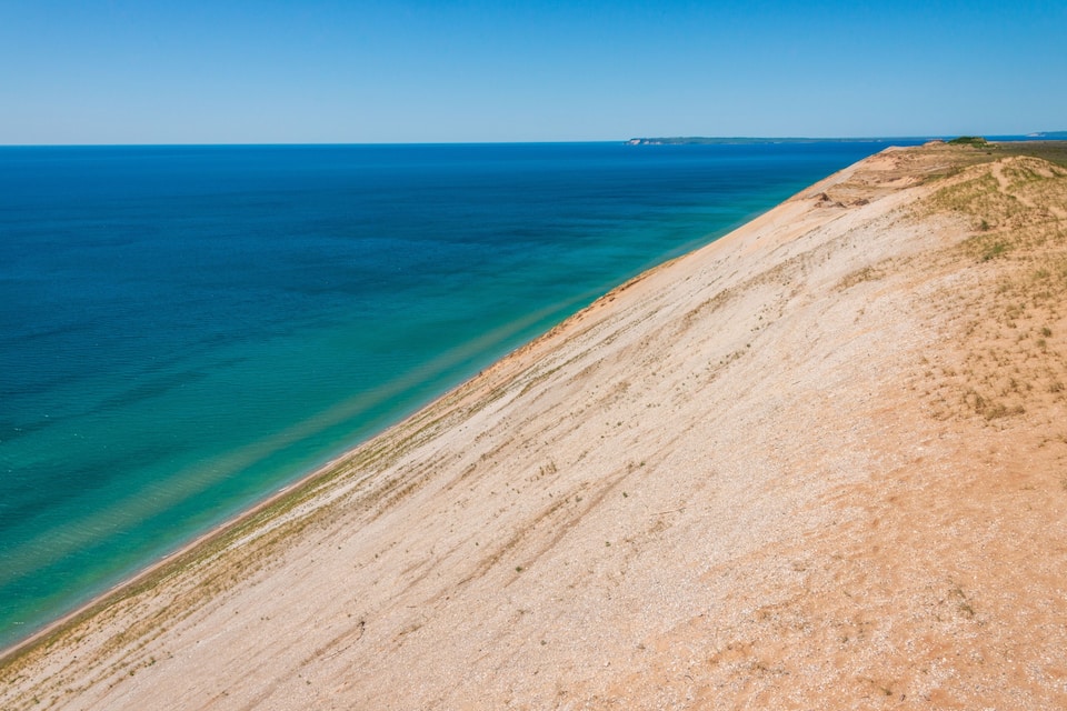 Paisagem costeira com praia de areia e águas azul-claras.