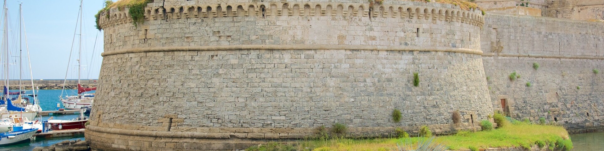 Um castelo de pedra histórico junto a um porto tranquilo com barcos.