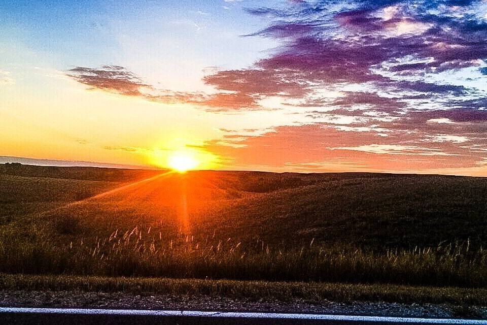 Pôr do sol sobre uma colina gramada com uma estrada em primeiro plano.