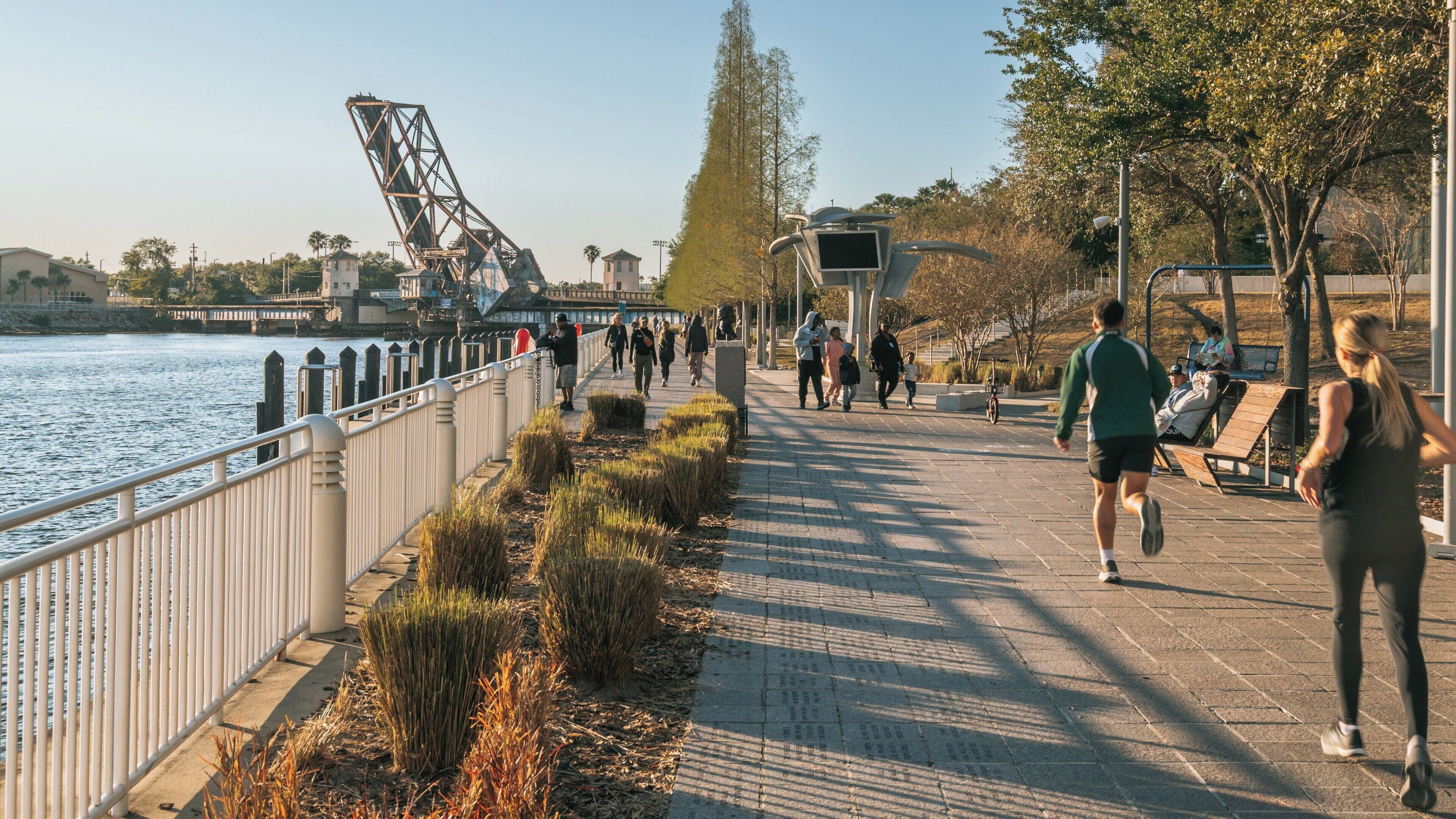 Bikers and joggers enjoying a sunny afternoon along the Tampa Riverwalk in Downtown Tampa, Florida, amidst picturesque waterfront views