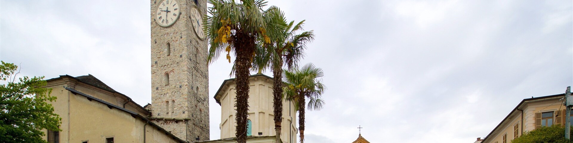 Uma igreja histórica com uma alta torre de sino, palmeiras e uma escadaria de pedra que leva à entrada.