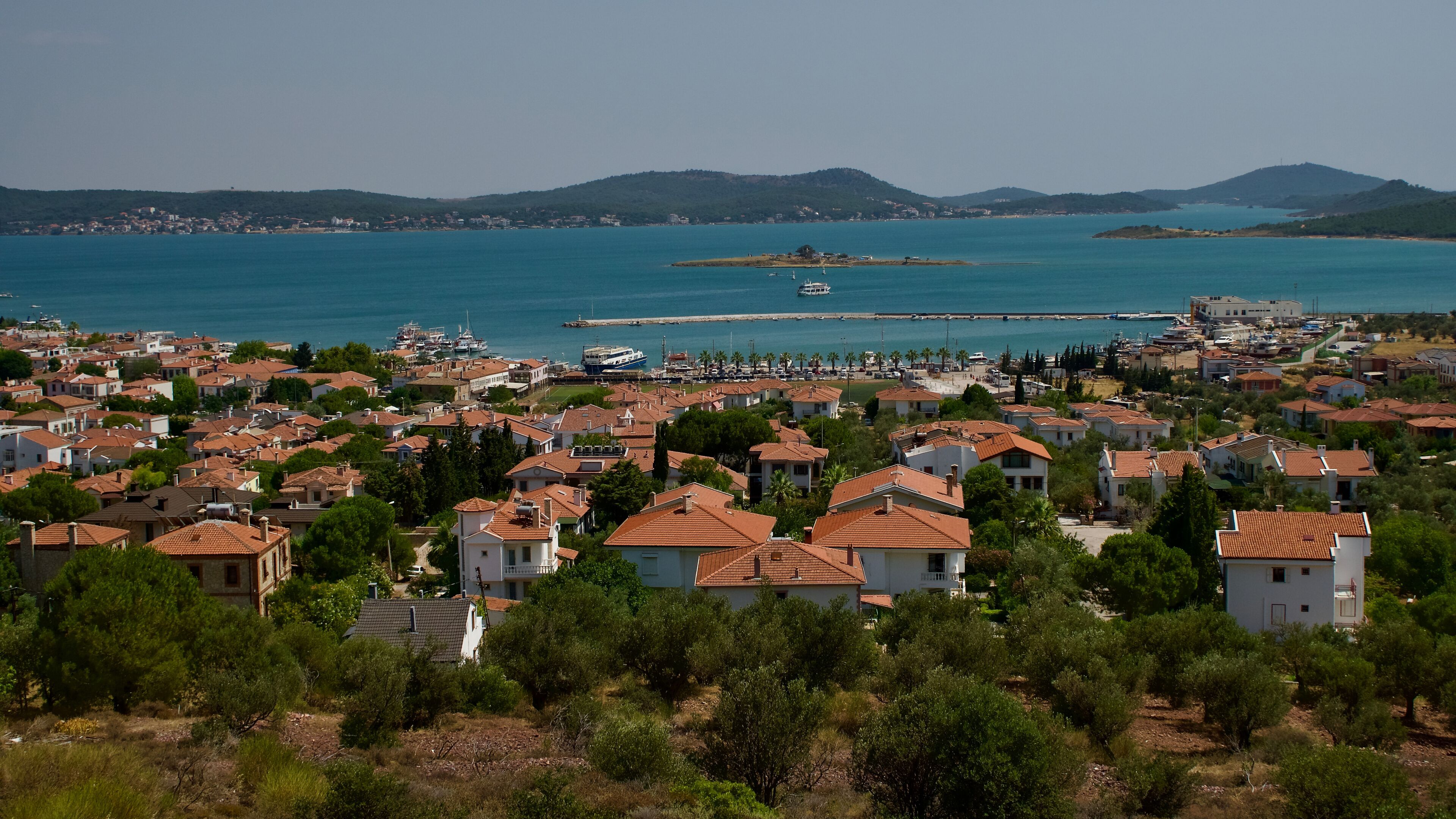 Uma vila costeira com casas de telhado vermelho, um porto e uma ilha ao longe.