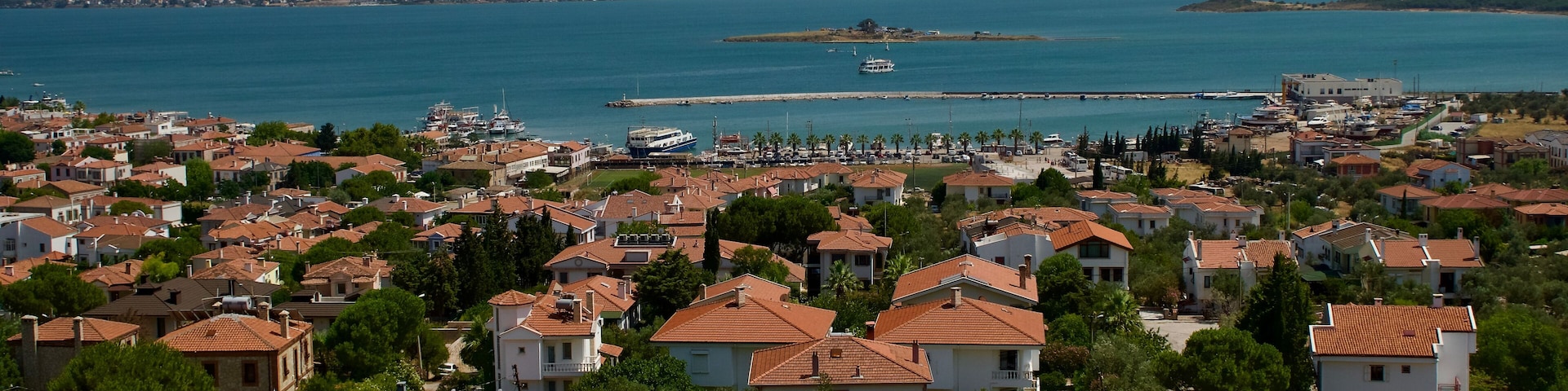 Uma vila costeira com casas de telhado vermelho, um porto e uma ilha ao longe.