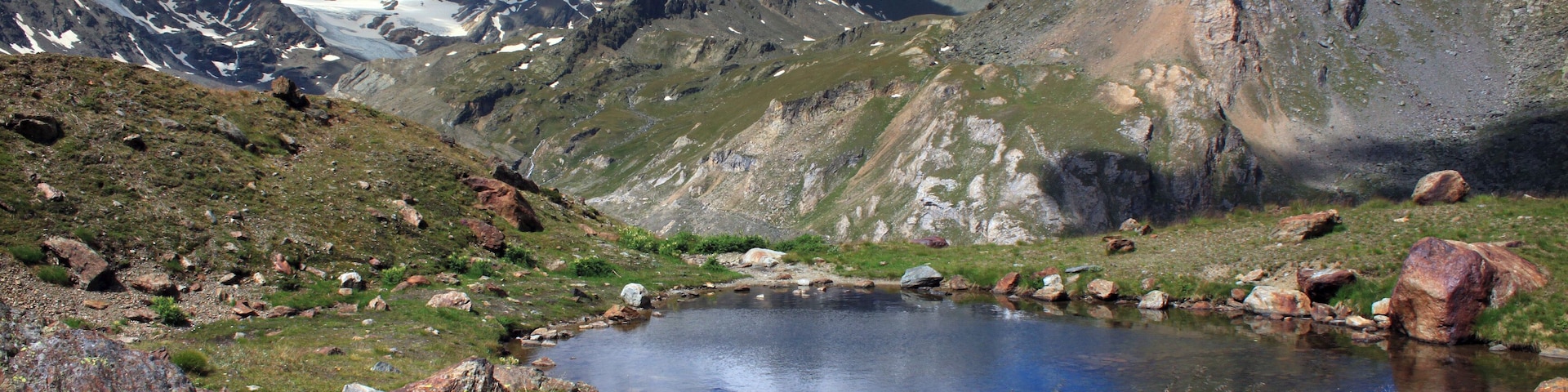 Paisagem montanhosa com um lago rodeado por pedras e vegetação.