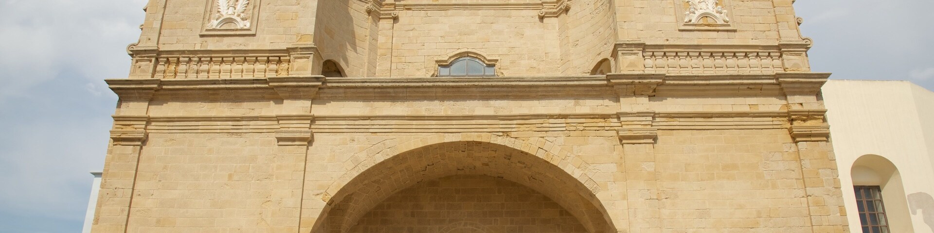 Um edifício histórico de pedra com detalhes arquitetônicos elaborados, incluindo uma grande entrada em arco e elementos decorativos sobre a porta.