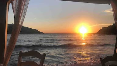 Pôr do sol sobre o mar, com cadeiras viradas para a paisagem.