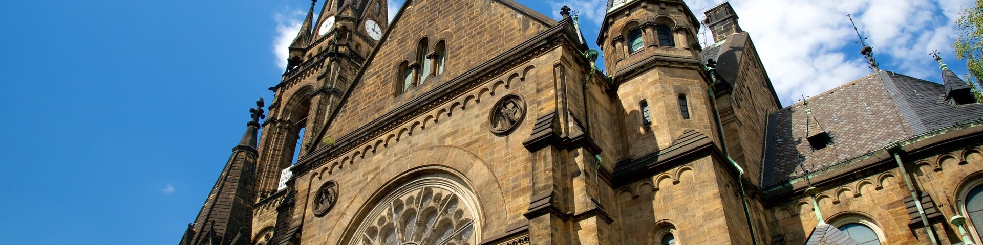Uma igreja histórica com uma grande torre de relógio, pináculos pontiagudos e detalhada fachada em pedra.
